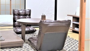 Um quarto com uma mesa redonda, duas poltronas de couro, um sofá e um tapete estampado.