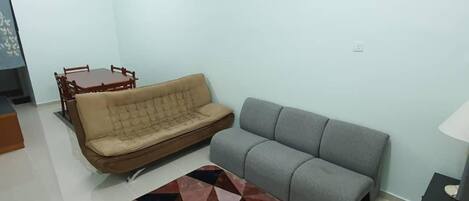 Uma sala de estar com um sofá marrom, um sofá cinzento, uma mesa de centro estampada e uma mesa de jantar com cadeiras.