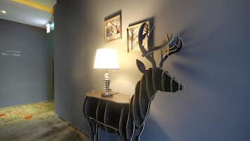 Um corredor com uma escultura de veado fixada na parede, uma luminária e duas obras de arte emolduradas.