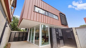 Uma casa moderna de dois andares com porta de entrada de vidro, alpendre coberto e portão preto.