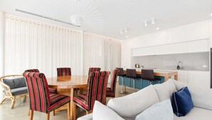 Uma sala de estar moderna com área de jantar, cozinha e uma grande janela com cortinas leves.