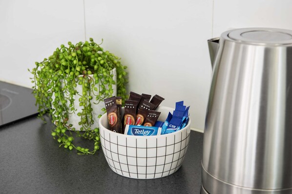 Uma bancada de cozinha com uma tigela branca estampada com padrão quadriculado, contendo barras de chocolate e uma chaleira.
