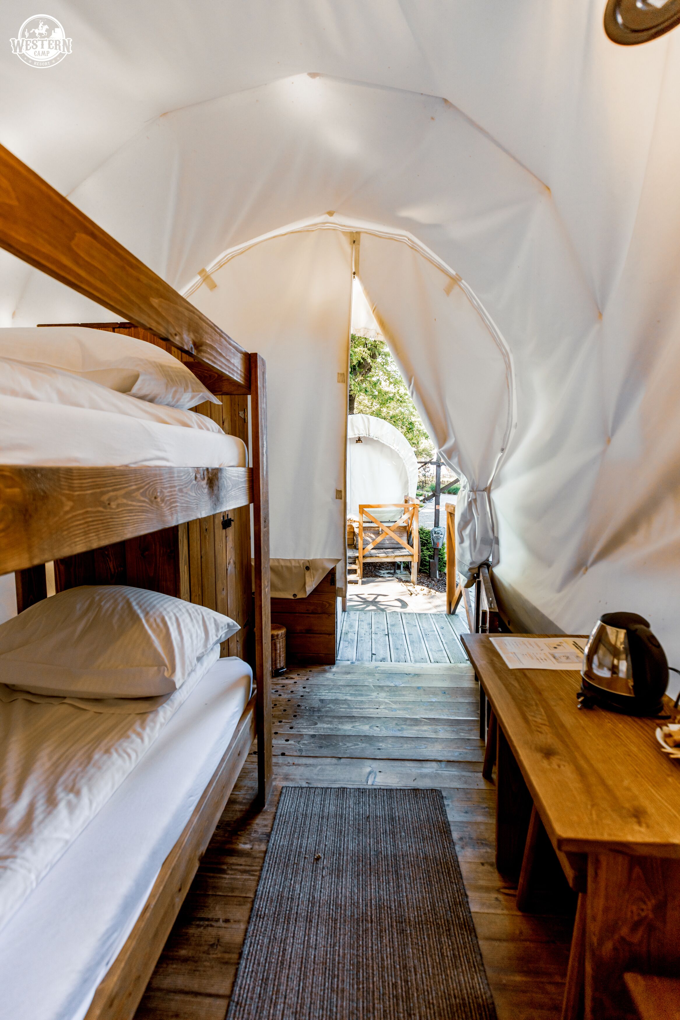 Alojamento em tenda com beliches, uma mesa de madeira e um banco.