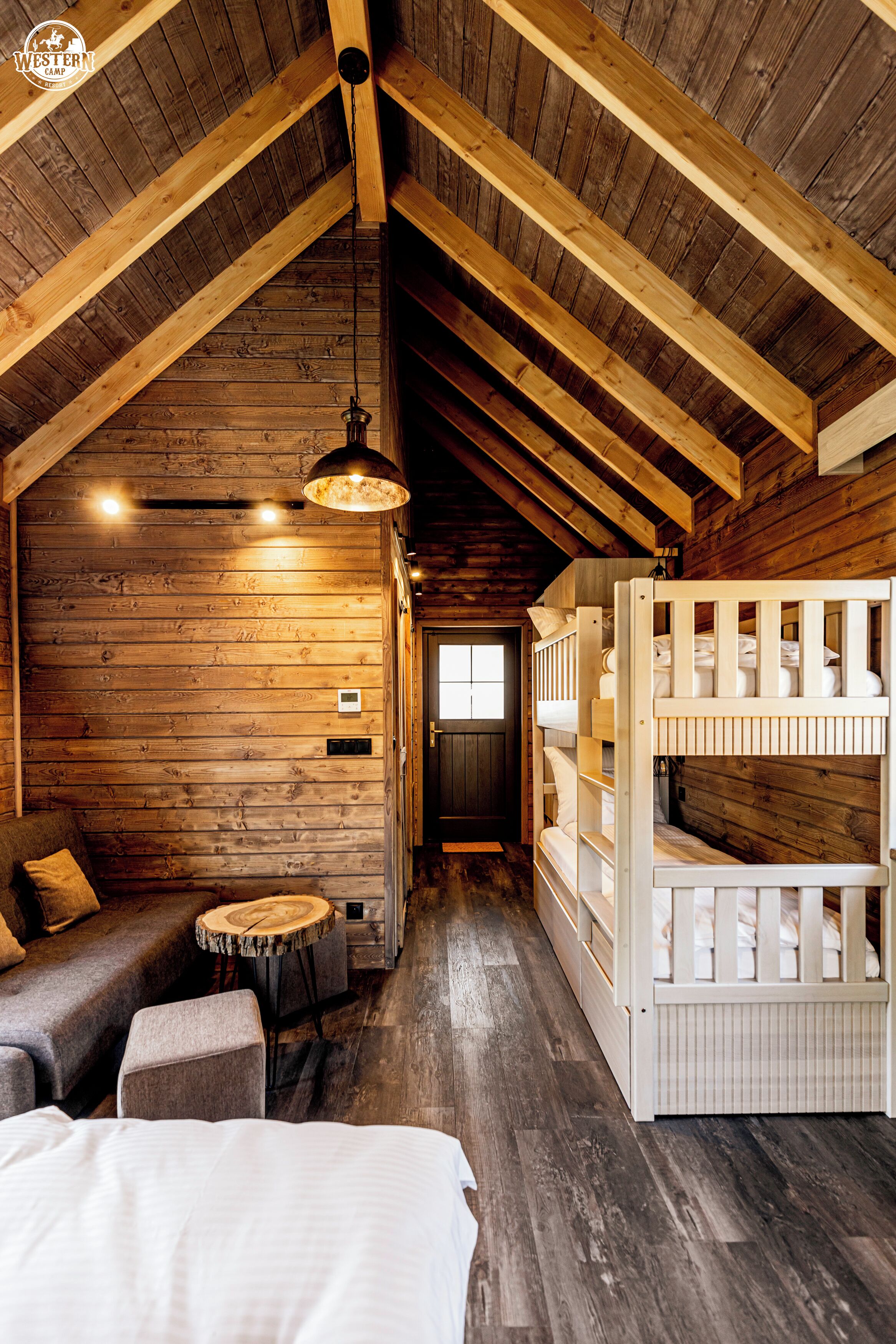 Interior rústico de cabana com paredes de madeira, cama em mezanino, sofá e mesa redonda.