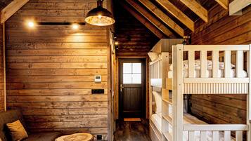 Interior rústico de cabana com paredes de madeira, cama em mezanino, sofá e mesa redonda.