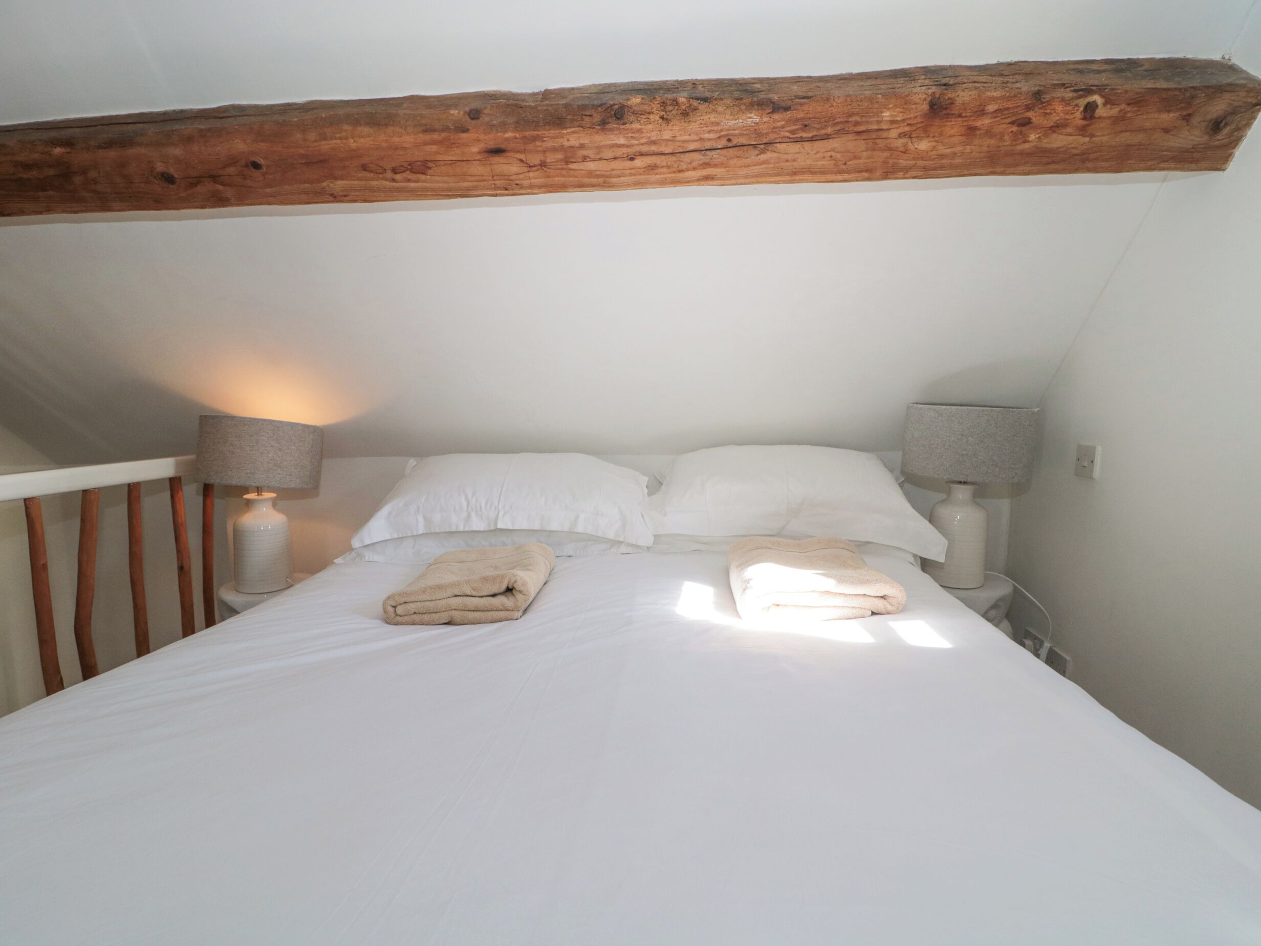 Quarto com teto de madeira, roupa de cama branca, duas almofadas e duas luminárias de cabeceira.