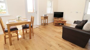 Uma sala de estar com piso de madeira, uma mesa de jantar com cadeiras, um rack para TV e um sofá.