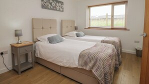 Quarto com duas camas, mesa de cabeceira com abajur, quadro na parede e janela com persianas.