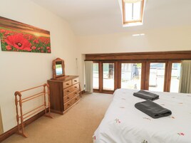 Um quarto com cama, cômoda, espelho, janela com cortinas e um quadro na parede.