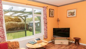 Uma sala de estar aconchegante com piso de madeira, um sofá, uma televisão e uma janela com vista para um jardim.