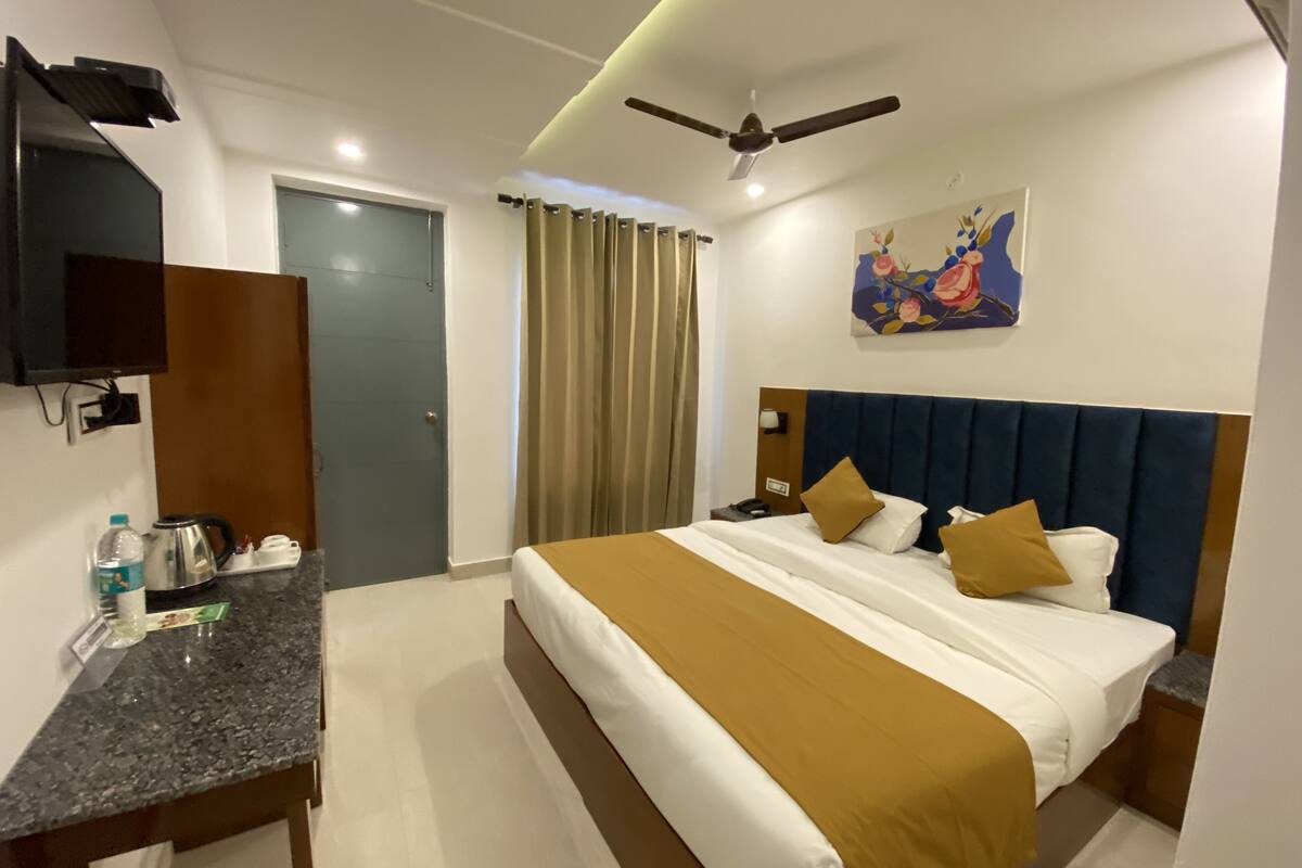 Quarto de hotel com cama, escrivaninha, cafeteira, televisão e ventoinha no teto.