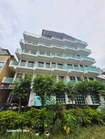 Um hotel com várias andares e varandas, rodeado por vegetação exuberante.