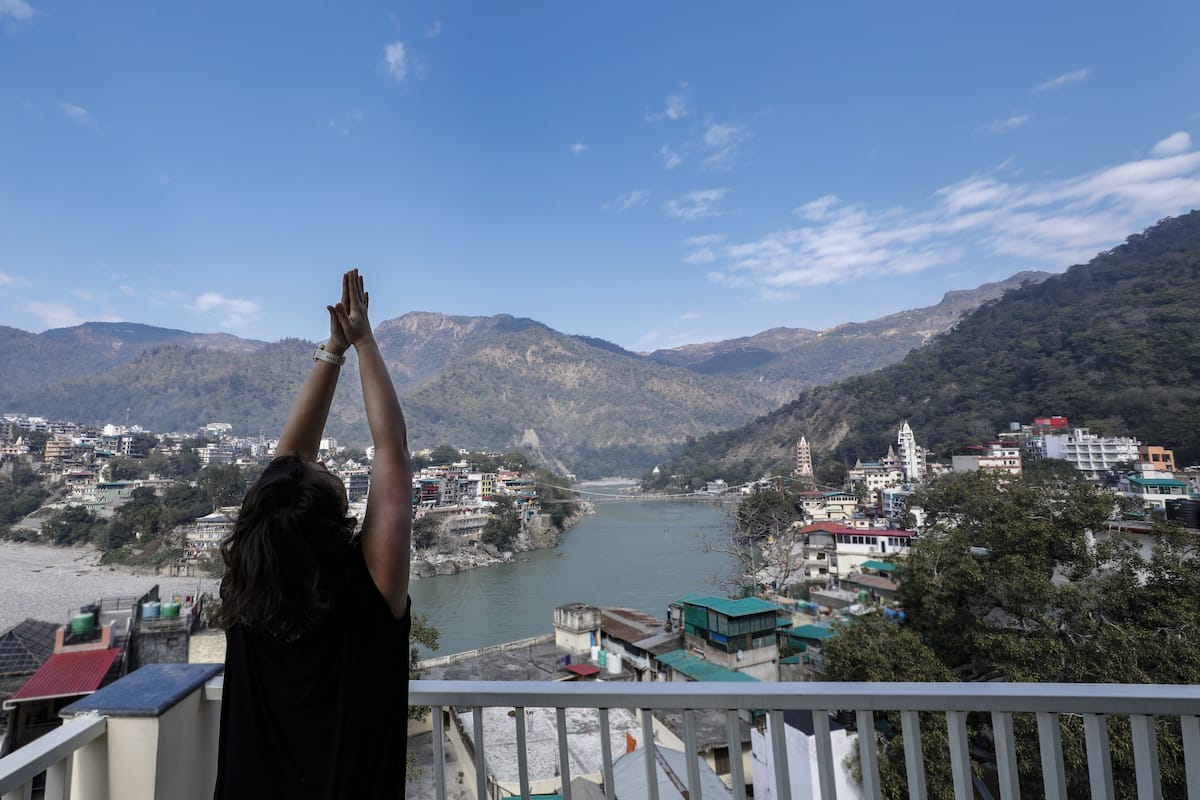 Uma pessoa em uma varanda com vista para um rio, montanhas e uma cidade.