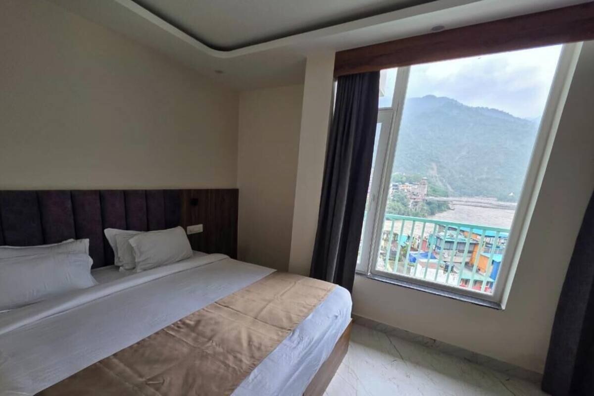 Quarto de hotel com uma cama grande, vista para uma paisagem montanhosa e uma varanda com guarda-corpo.