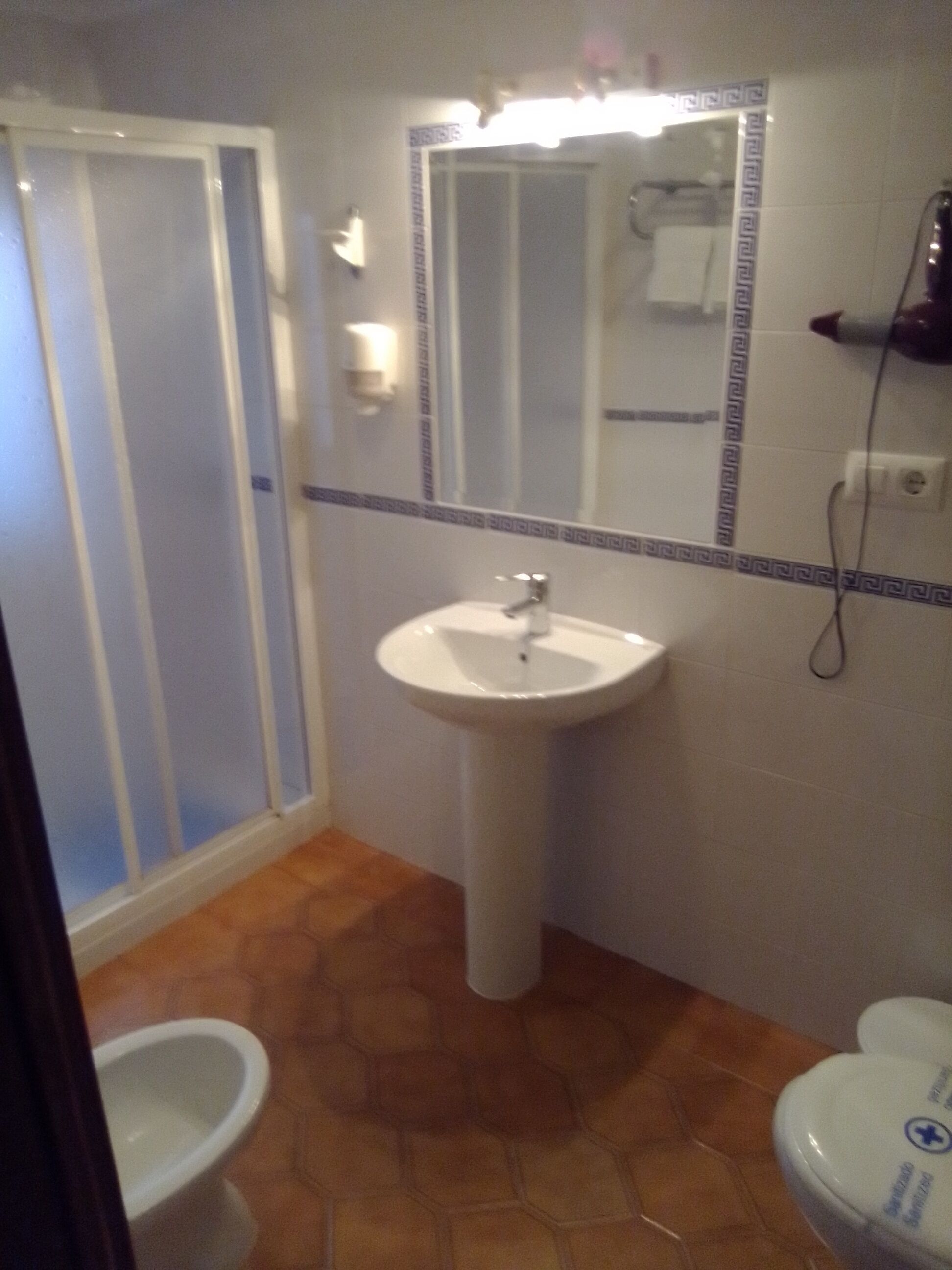 Uma casa de banho com uma pia branca, um espelho, uma sanita e uma cabine de duche.