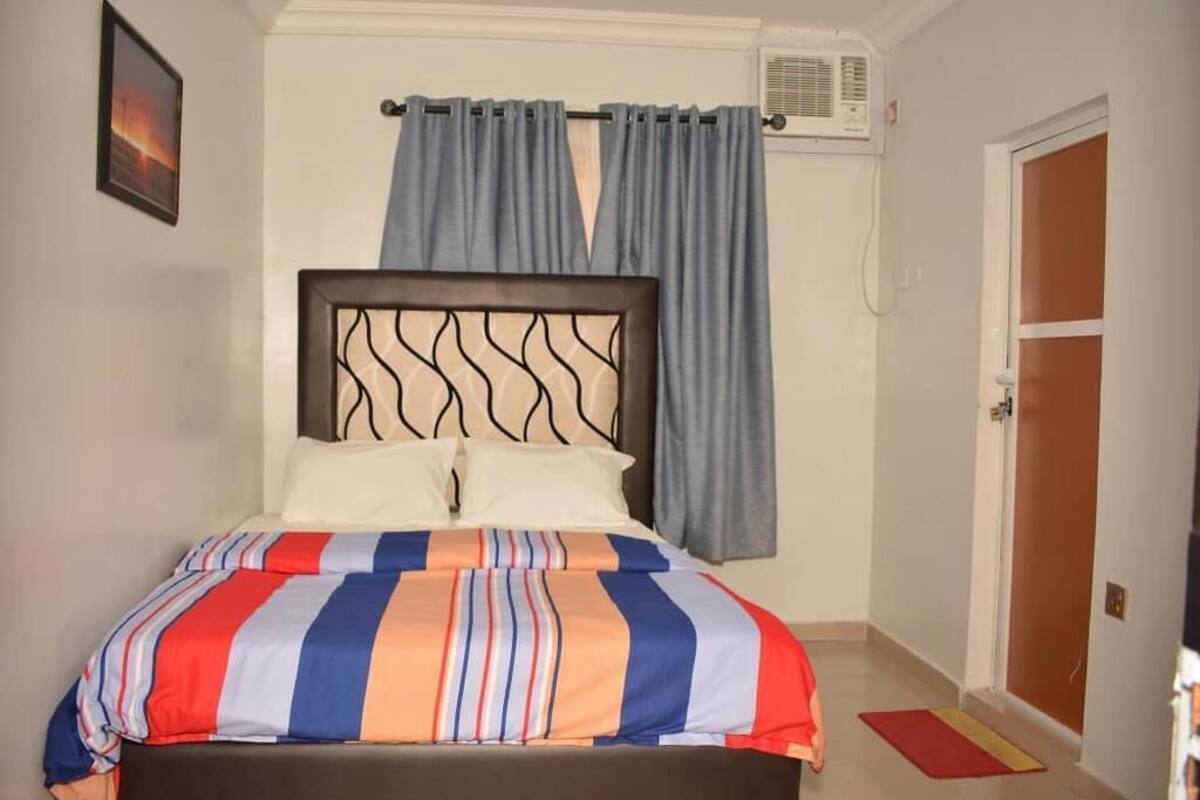 Uma cama com colcha listrada, cabeceira com design ondulado e cortina azul.