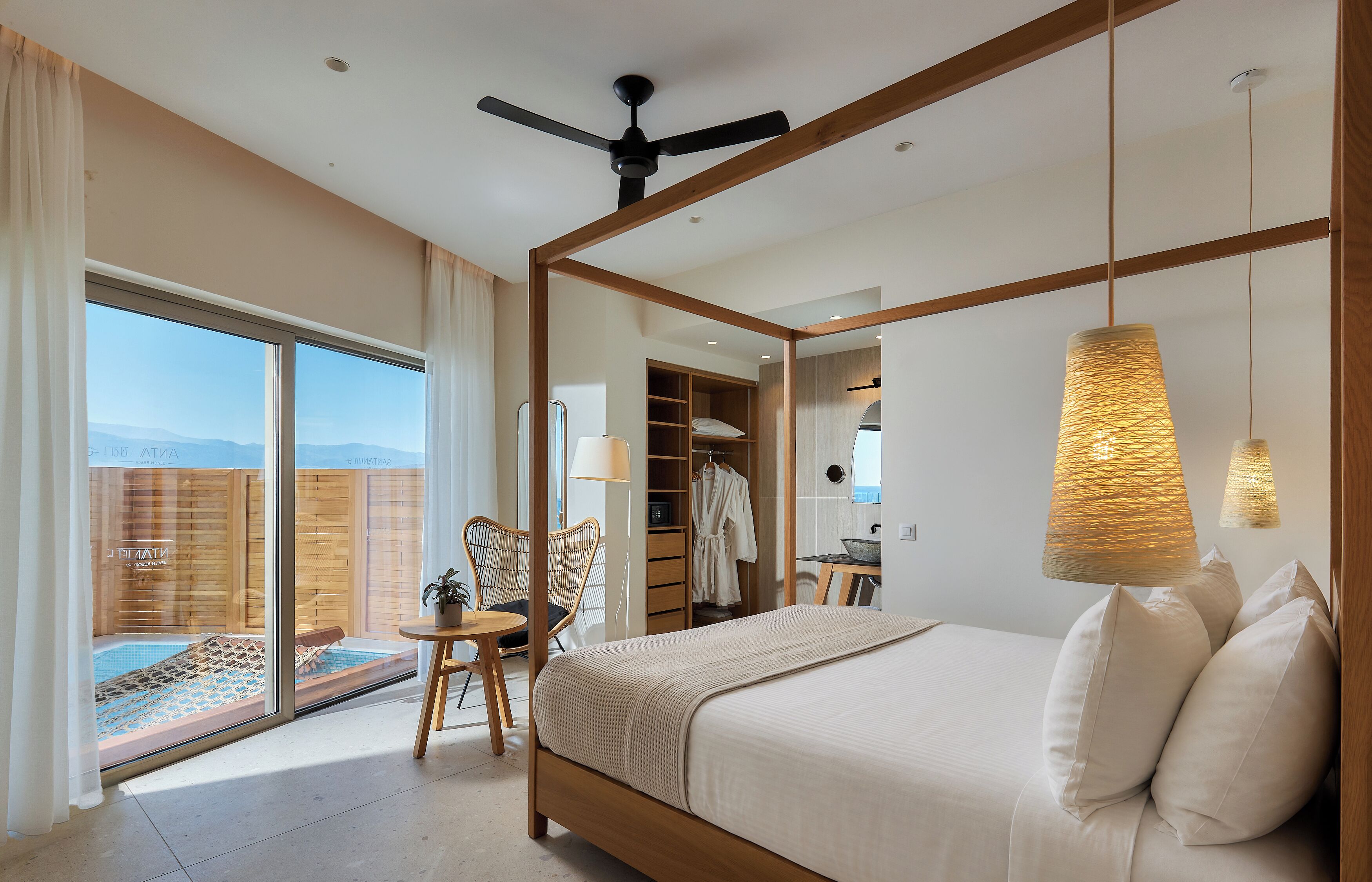 Quarto com cama grande, ventilador de teto, vista para uma piscina e estrutura de teto em madeira.