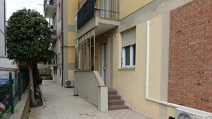 Uma passagem estreita com um edifício de um lado e uma árvore do outro. Uma escadaria leva a um nível superior.