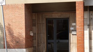 Entrada de edifício com fachada de tijolos, porta de vidro e placa numerada.