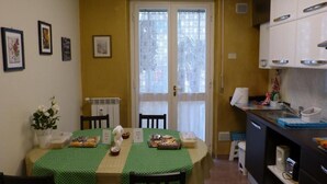 Uma sala de jantar com uma mesa posta para dois, uma cozinha com armários brancos e uma porta com painéis de vidro fosco.