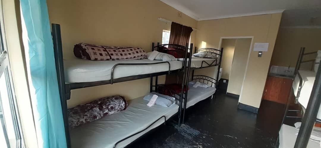 Um dormitório com beliches, uma janela com cortinas e uma porta que dá para outro quarto.