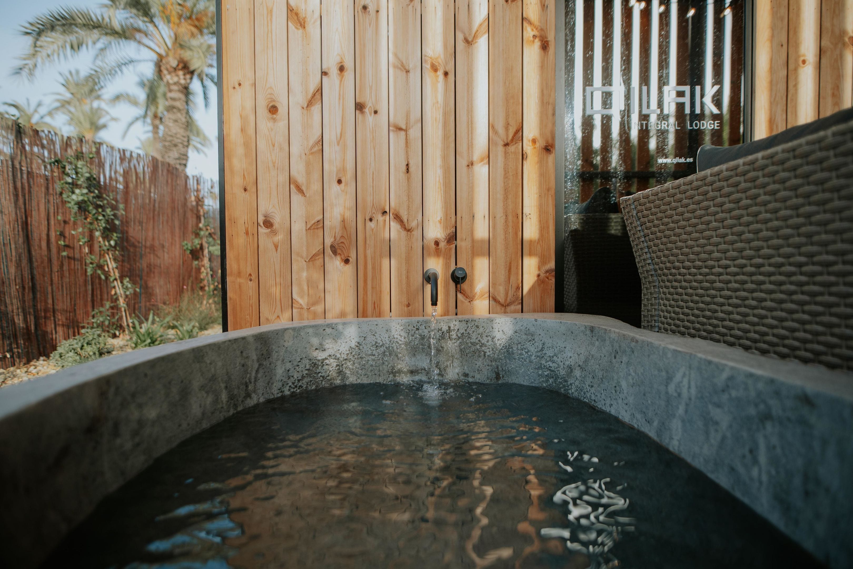 Uma área de spa em madeira com banheira de hidromassagem, mobiliário de vime e um cercado de madeira ao fundo.