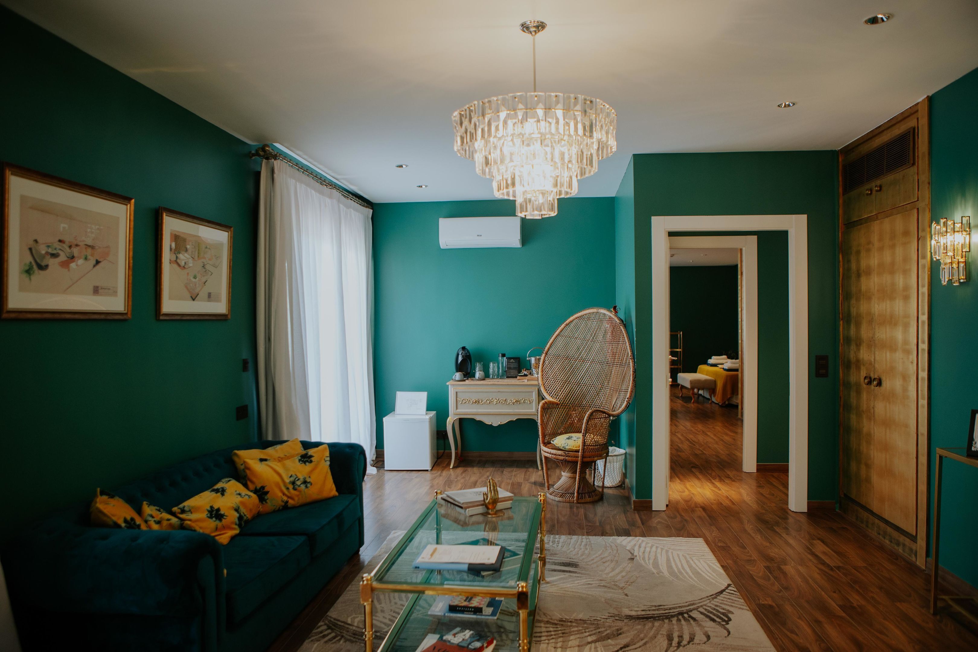 Uma sala de estar com paredes verde-água, um sofá azul, uma mesa de centro de vidro e um lustre.