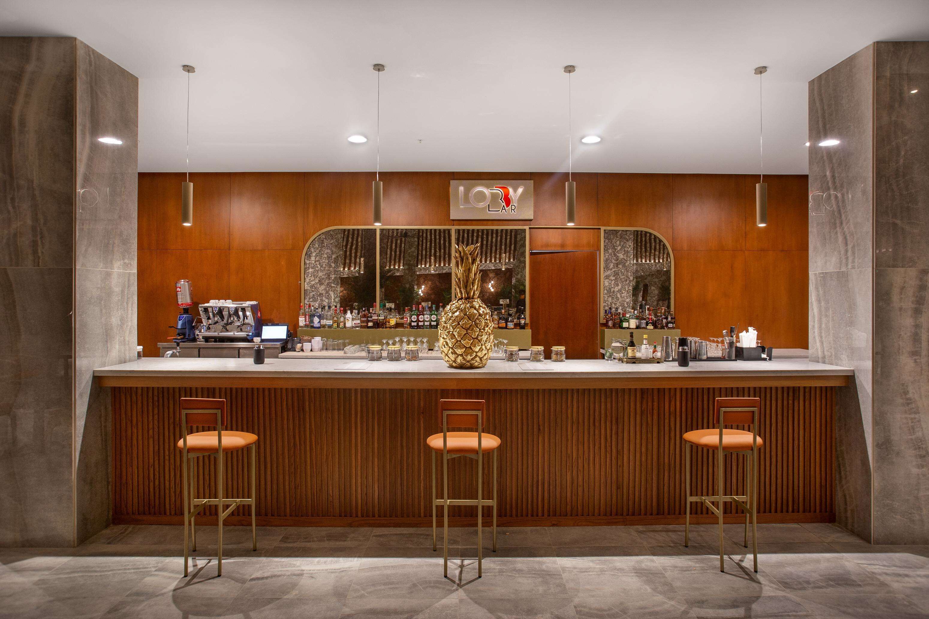 Uma área de bar com balcão de madeira, três banquetas e uma placa que diz 'LOBY BAR'.