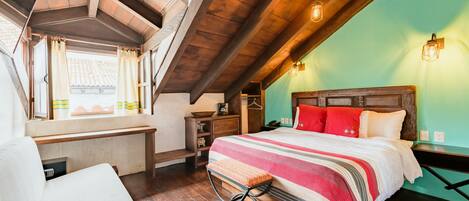 Um quarto de sótão acolhedor com teto de madeira, cama com roupa de cama vermelha e branca, escrivaninha com cadeira e luminária suspensa.