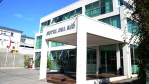Um hotel moderno com entrada ampla, janelas grandes e uma placa visível com a inscrição "HOTEL DEL RIO".