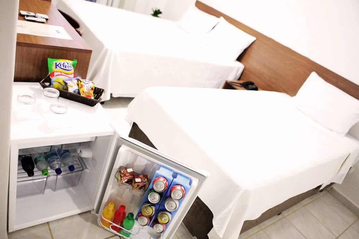 Quarto de hotel com duas camas, um minibar e uma pequena mesa com petiscos e bebidas.