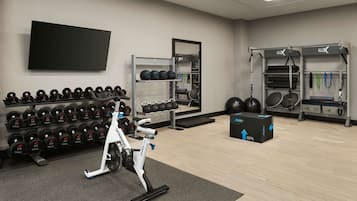 Uma academia com equipamentos de exercícios, incluindo halteres, uma bicicleta ergométrica e um suporte para pesos.