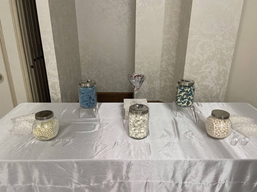 Uma mesa com cinco potes de vidro contendo vários objetos, uma taça de martini e uma pequena caixa branca.