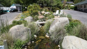 Um jardim tranquilo com um pequeno riacho, pedras grandes e um banco branco.