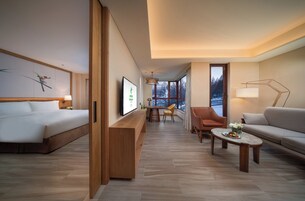 Quarto de hotel moderno com cama, sofá, área de refeições e vista para uma paisagem coberta de neve.