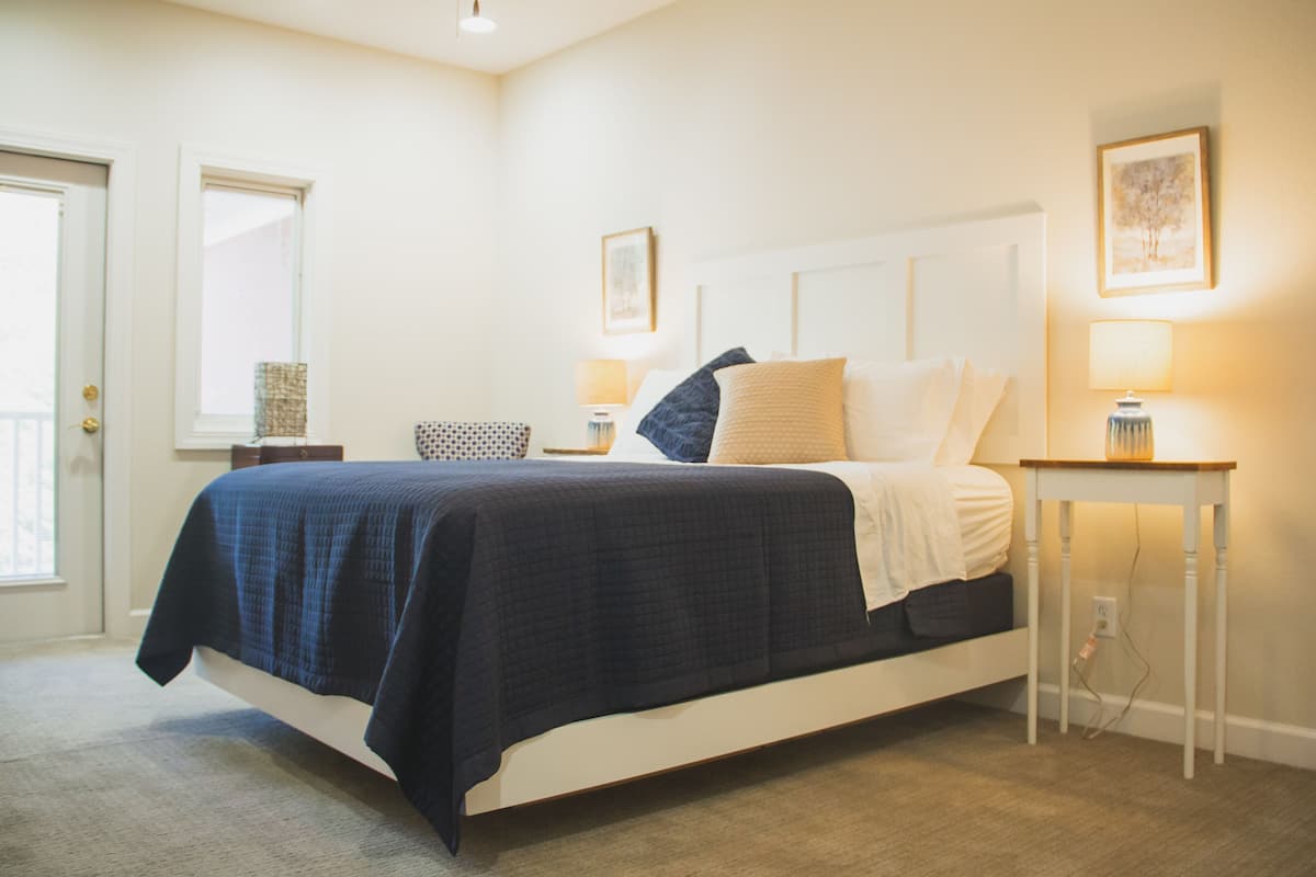 Quarto com cama, mesas de cabeceira e luminárias fixadas na parede.