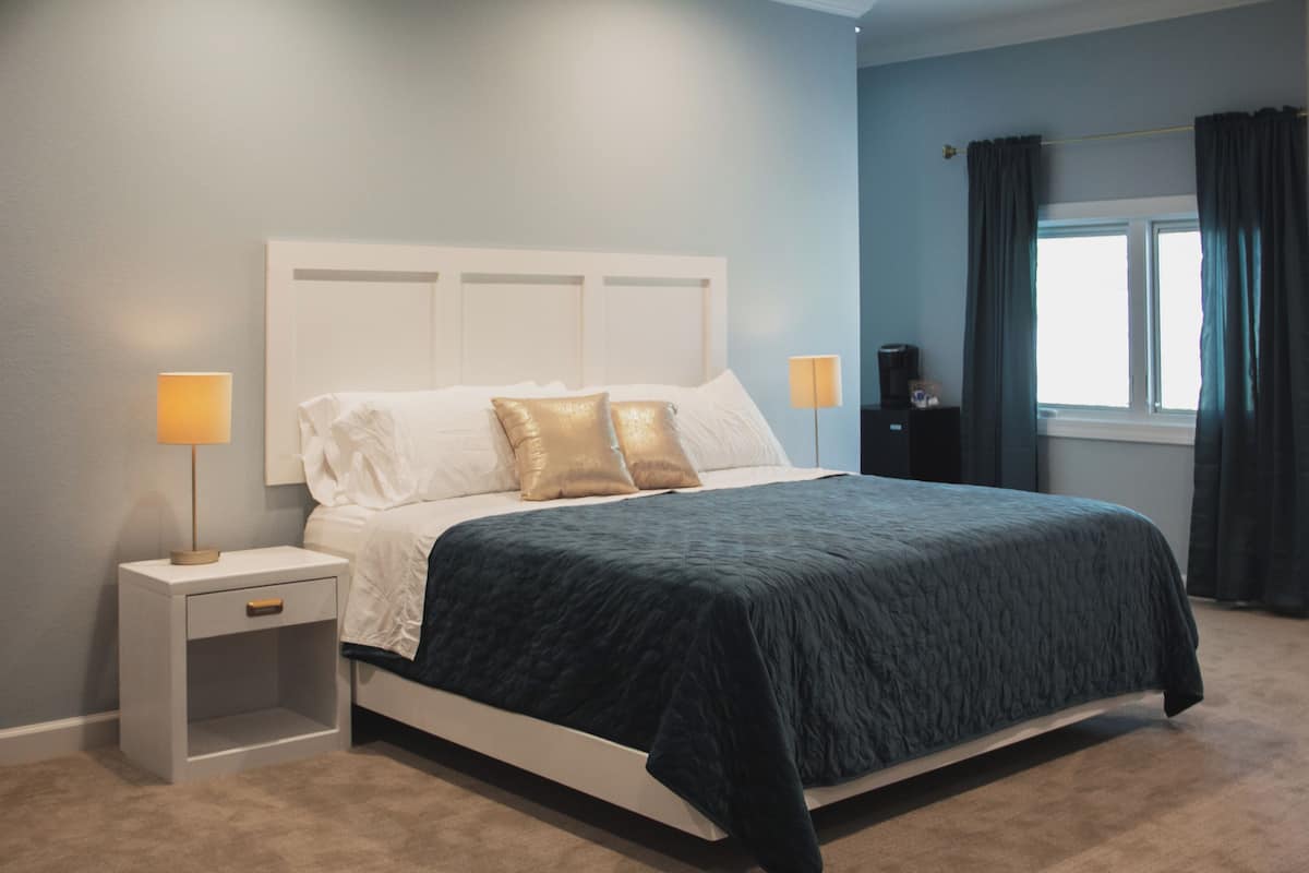 Quarto bem organizado com cama, abajures e janela com cortinas.