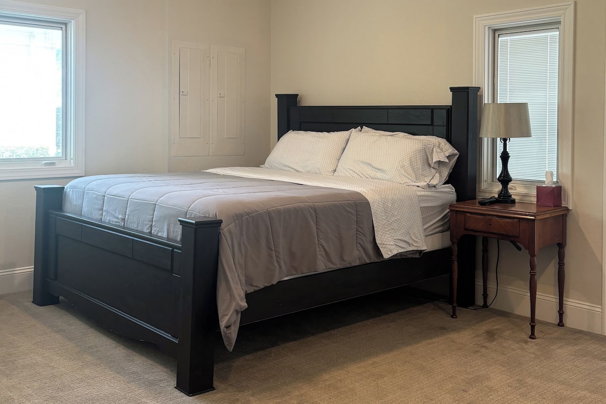 Quarto com cama, mesa de cabeceira, abajur e janela.
