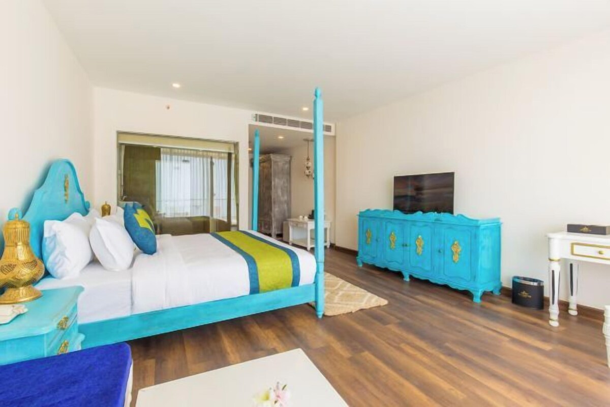 Quarto com cama, penteadeira azul, televisão e escrivaninha.