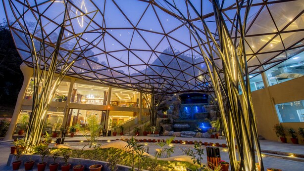 Um edifício moderno com estrutura em cúpula de vidro, plantas em interior e uma cascata.