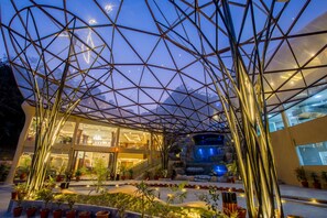 Um edifício moderno com estrutura em cúpula de vidro, plantas em interior e uma cascata.