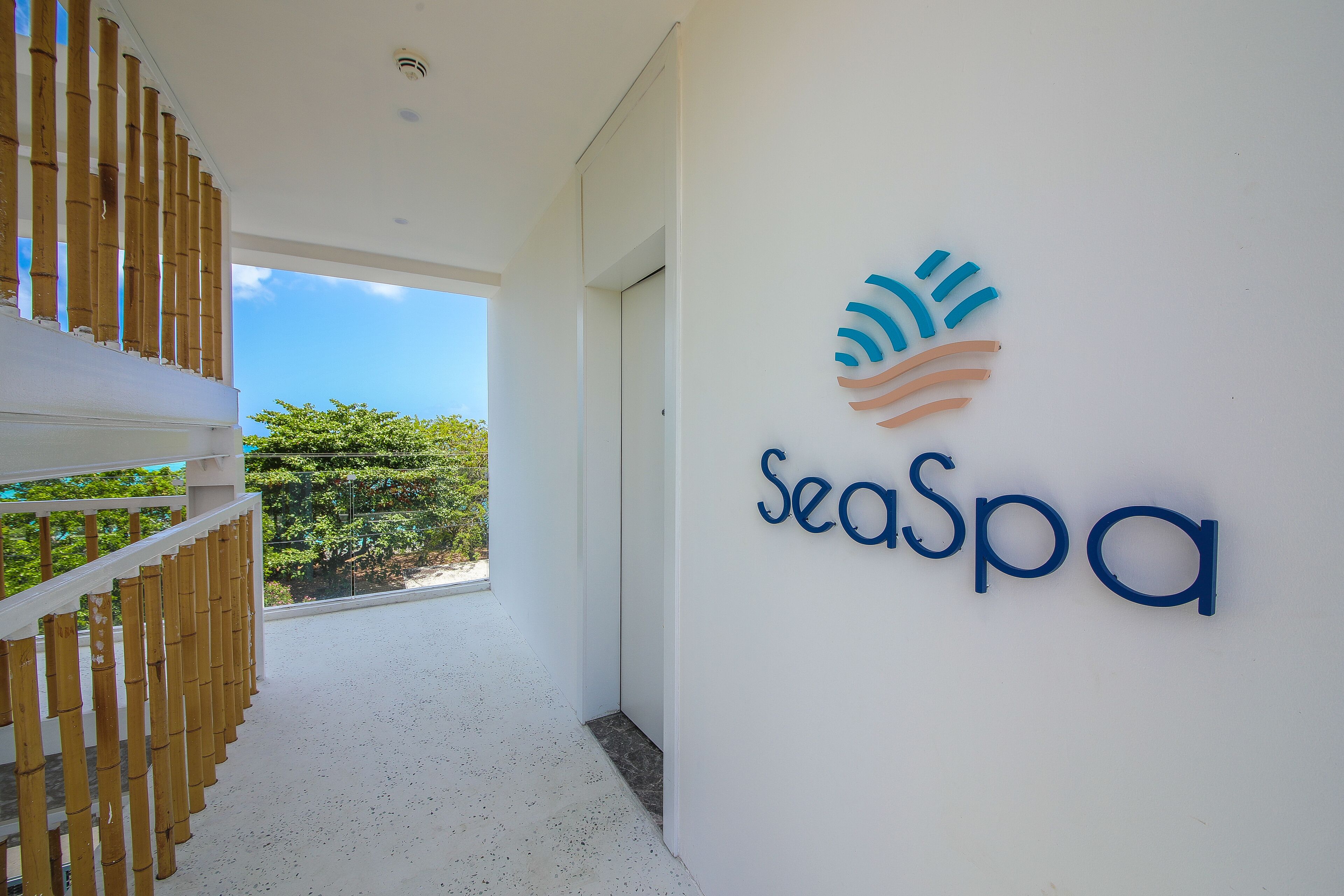 Corredor que leva a uma área de spa, com uma placa indicando "SeaSpa" e vista para o verde lá fora.