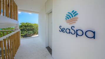 Corredor que leva a uma área de spa, com uma placa indicando "SeaSpa" e vista para o verde lá fora.