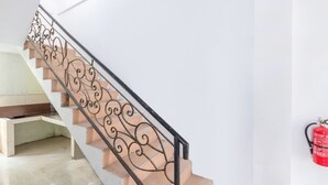 Uma escadaria com corrimãos de metal ornamentados e um extintor fixado na parede.