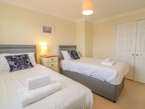 Quarto de hotel com duas camas, uma mesinha de cabeceira com abajur, um quadro emoldurado na parede e uma porta branca.
