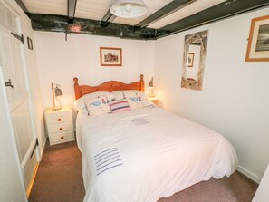 Quarto com cama de madeira, duas mesas de cabeceira com luminárias, uma porta branca e um quadro pendurado na parede.