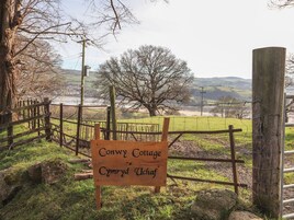 Placa de madeira com o texto 'Conwy Cottage' e 'Cymru Uchaf', indicando o nome da propriedade.