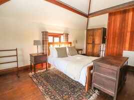 Um quarto com cama de madeira, mesa de cabeceira, cômoda, janela com cortinas e radiador.