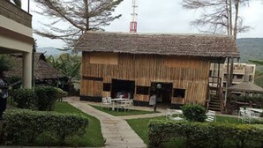 Um edifício rústico com telhado de colmo, rodeado por um jardim bem cuidado e um caminho pavimentado.