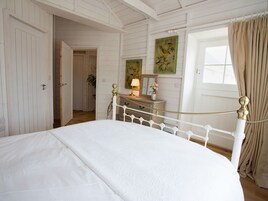 Quarto com cama branca, penteadeira com espelho e um quadro na parede.